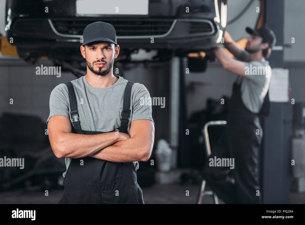 professional mechanic in overalls with crossed arms, while colleague ...