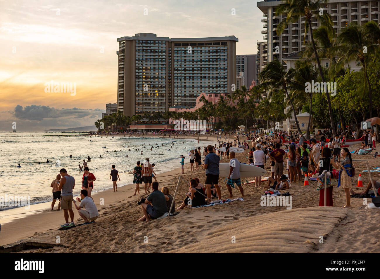 The iconic Waikiki Beach at sunset with a crowd of people appreciating ...