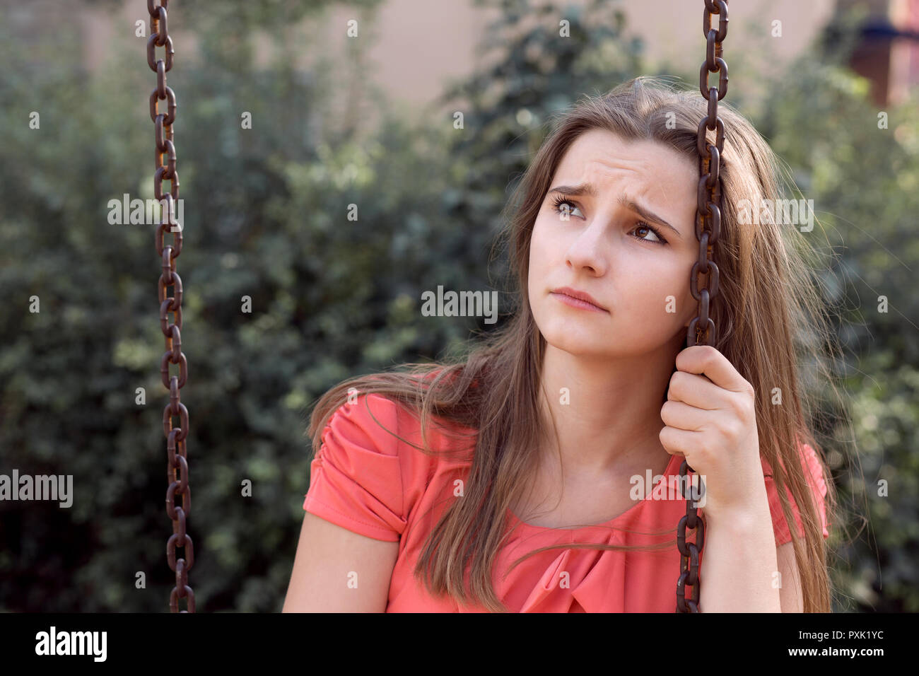Sad unhappy teen girl with long brunette hair sitting on a swing sadly ...