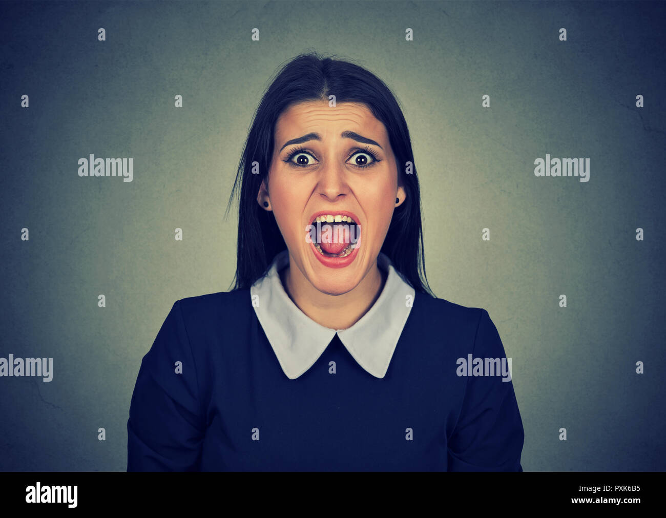 Adult brunette in dress yelling at camera with rage on gray background ...