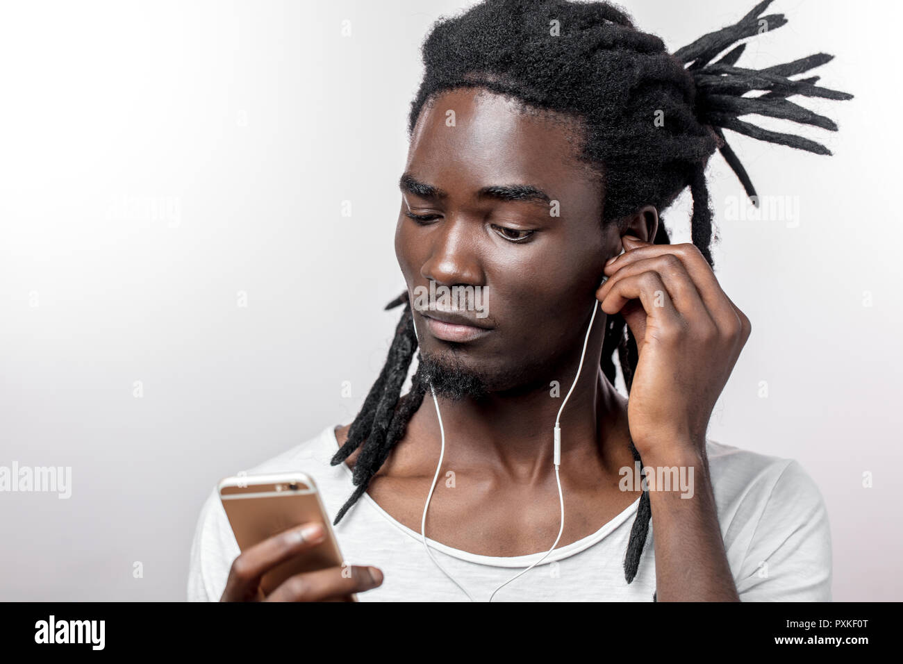 African man wearing headphones and holding his smartphone against white ...