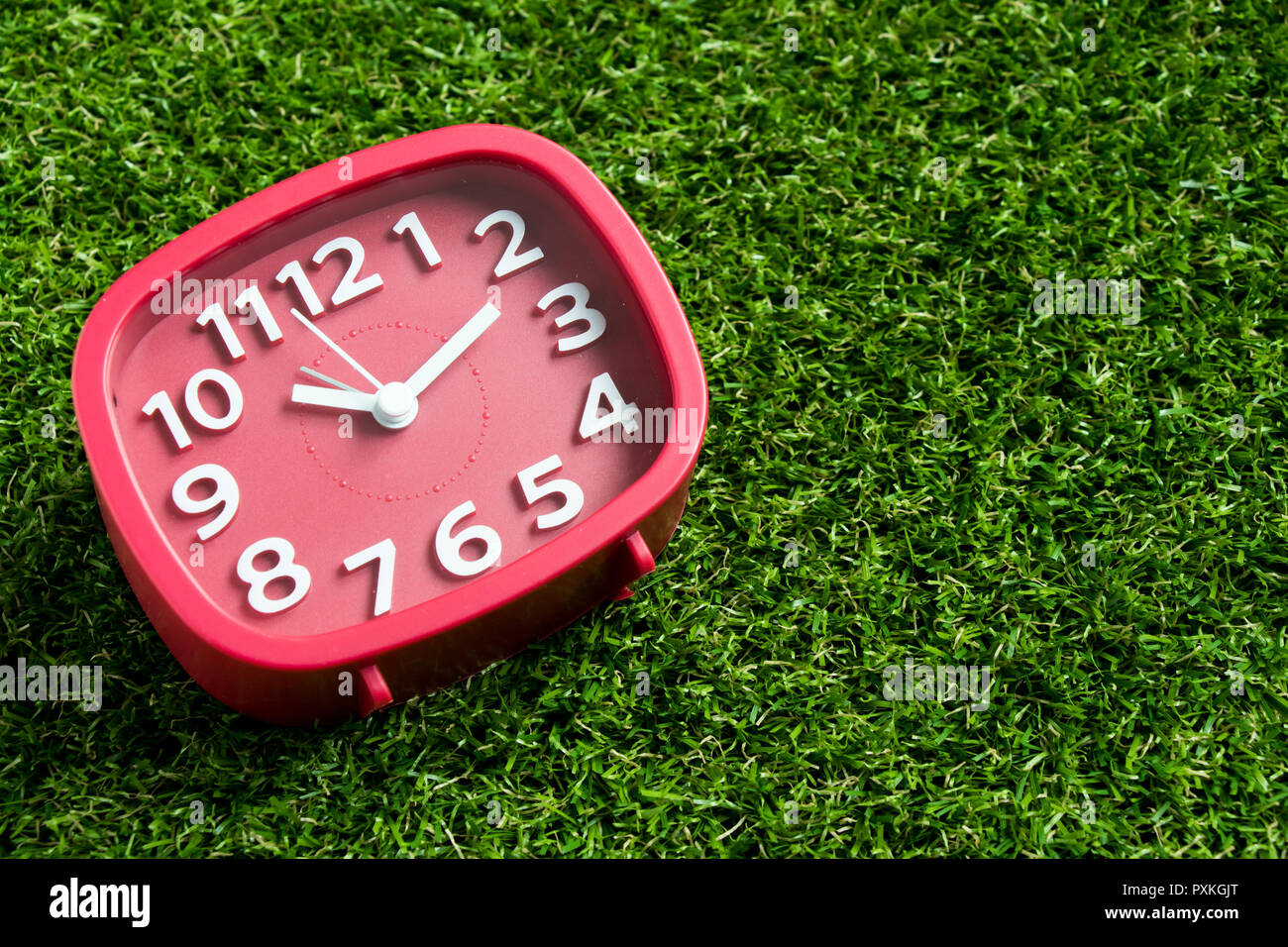 Red analog clock on artificial green grass background Stock Photo - Alamy