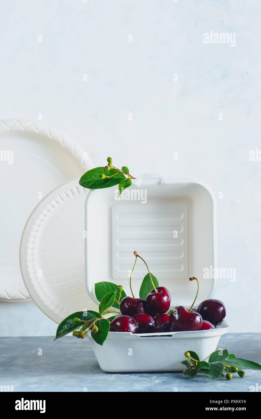 Eco-friendly food packaging with cherries. White containers, plates and ...