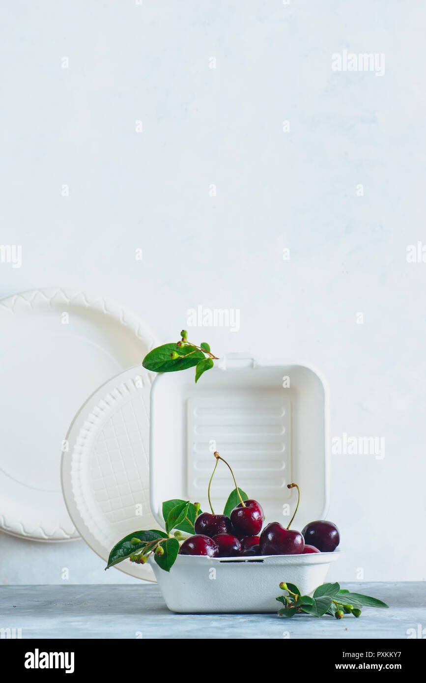 Eco-friendly food packaging with cherries. White containers, plates and ...