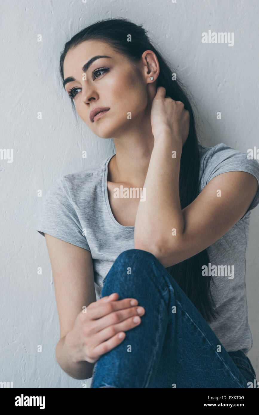 depressive attractive brunette girl sitting and looking away on grey ...