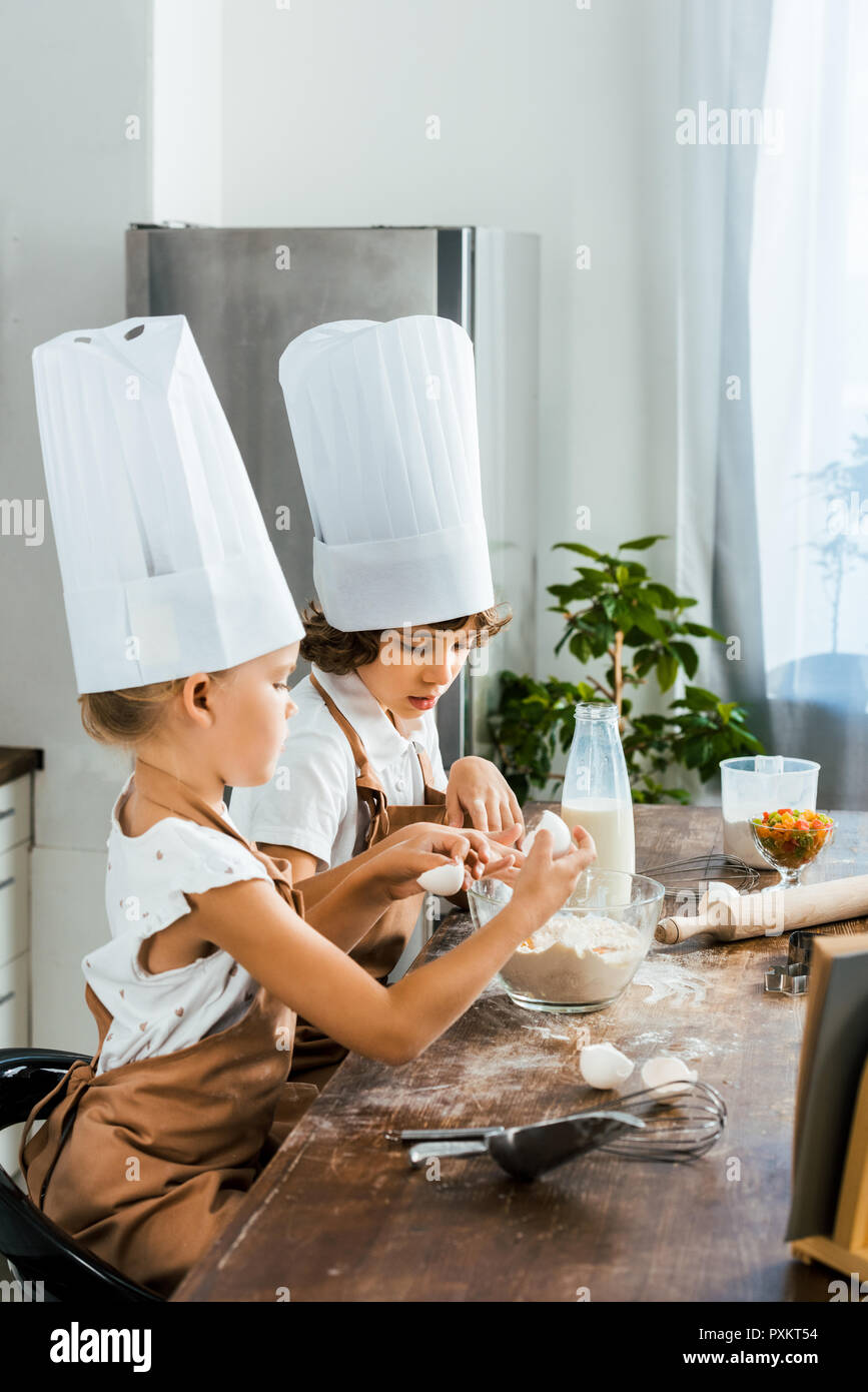 side view of cute little children in chef hats and aprons preparing ...