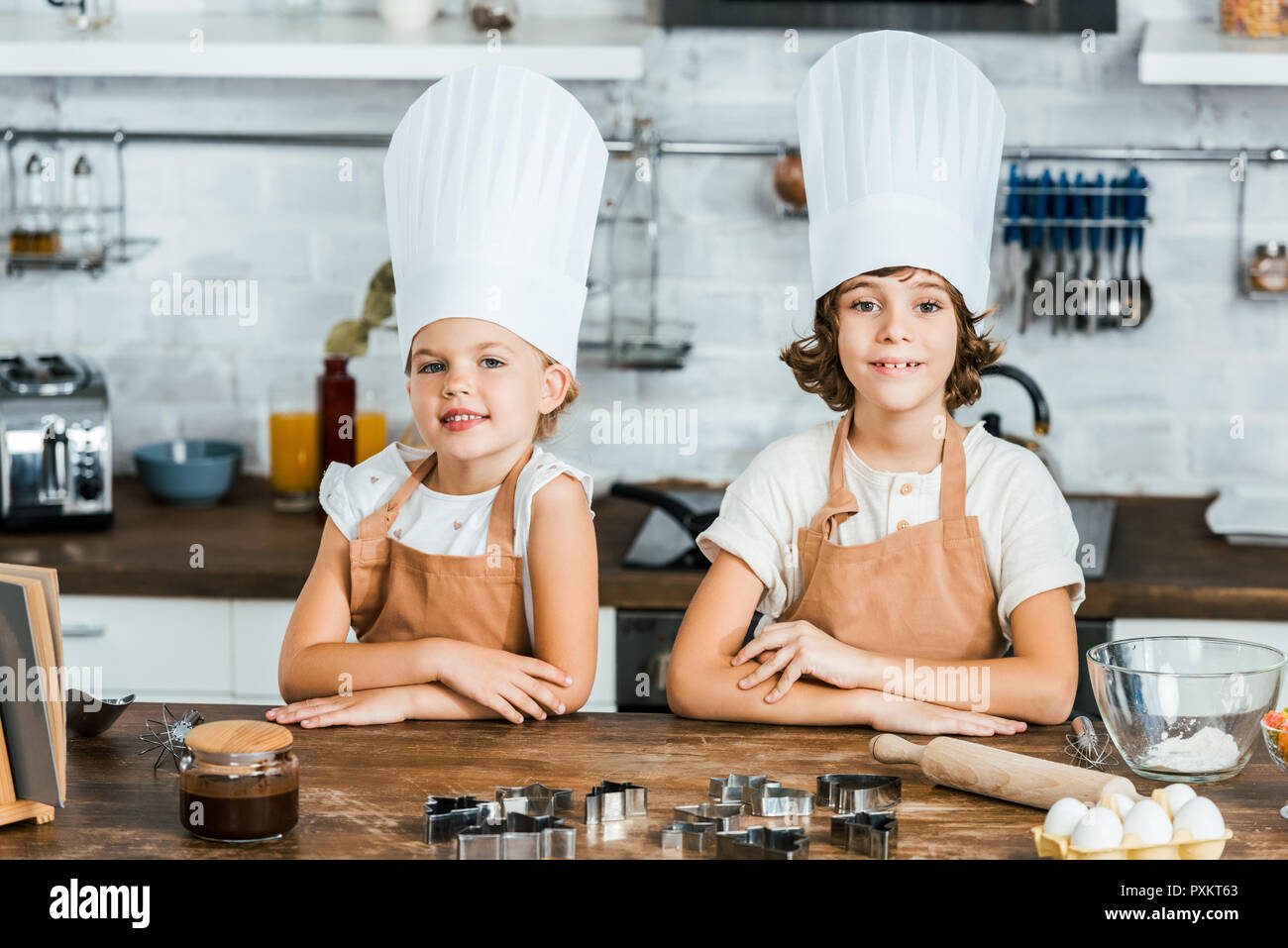cute happy children in aprons and chef hats smiling at camera while ...