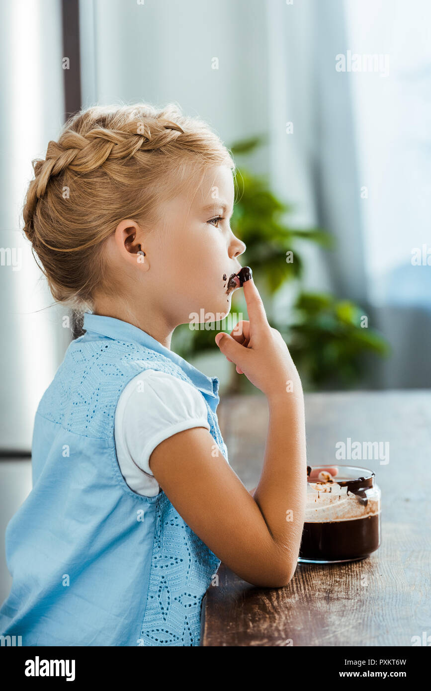 side view of cute little child eating delicious chocolate spread and ...