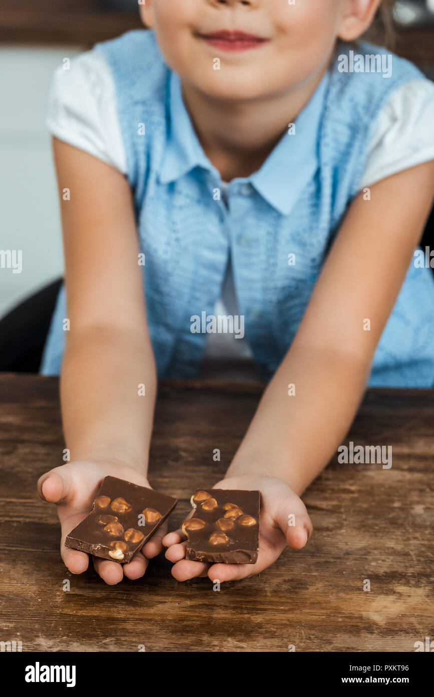 close-up partial view of smiling child holding pieces of sweet ...