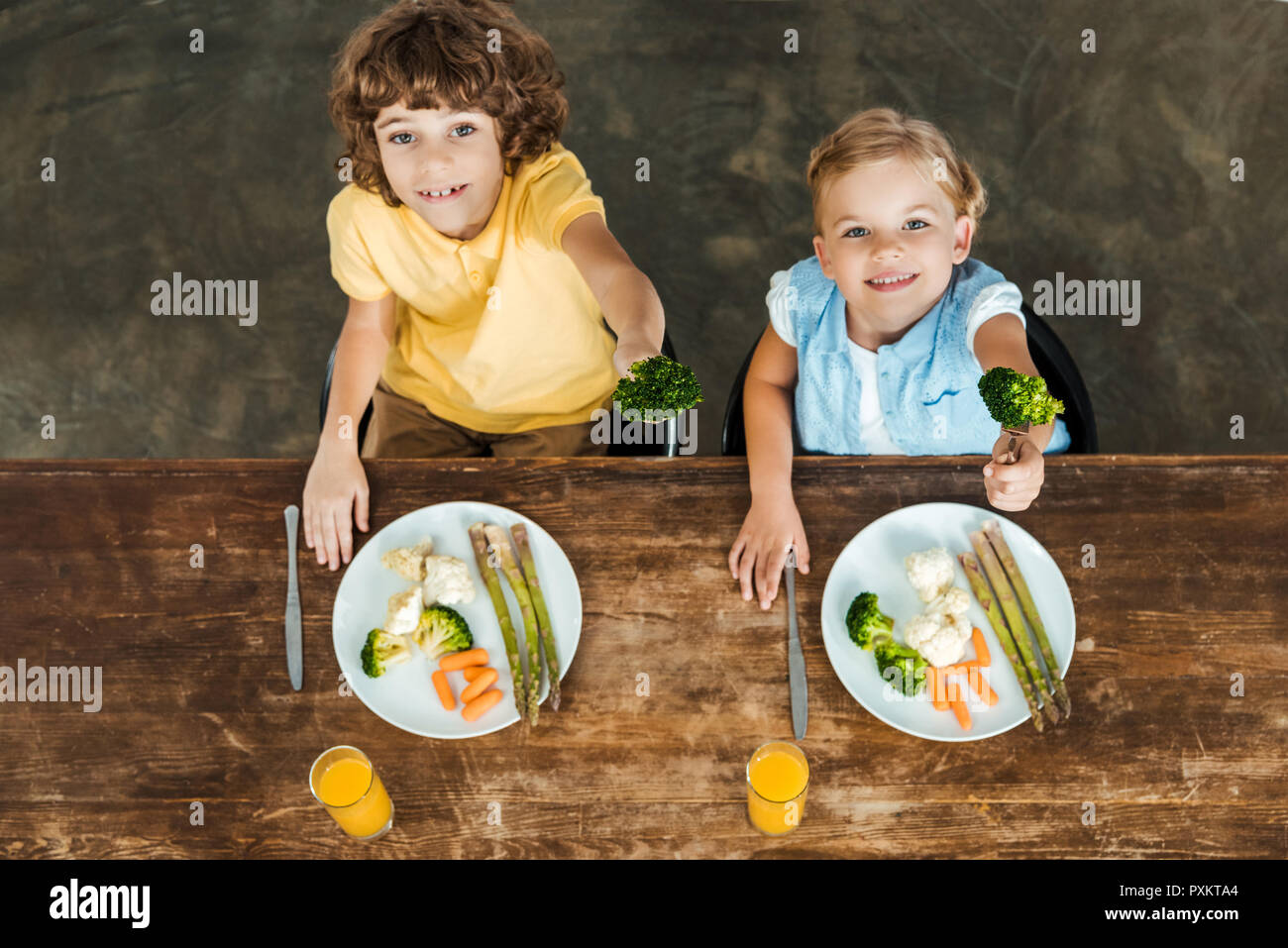 high angle view of cute happy children holding forks with broccoli and ...