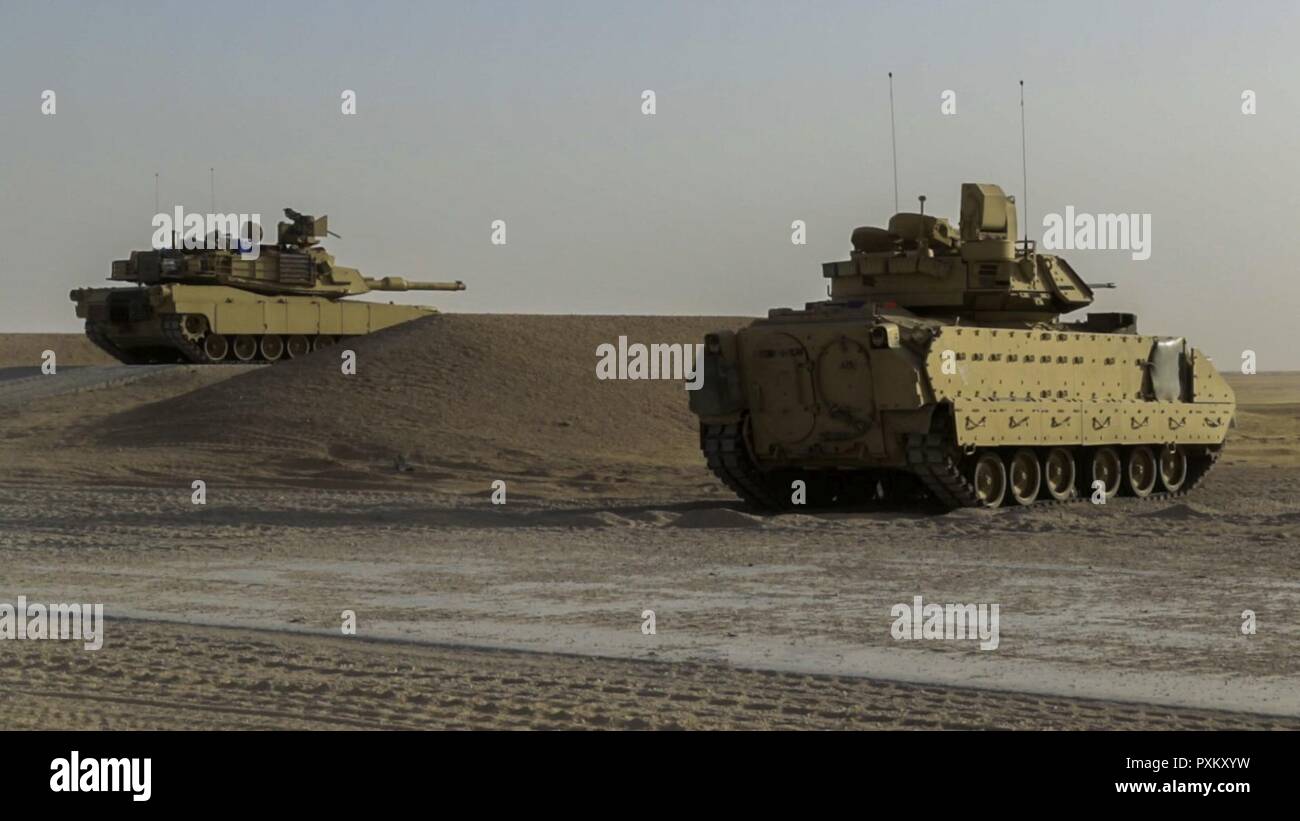 An M1A2 Abrams tank (left) prepares to fire a round while receiving ...