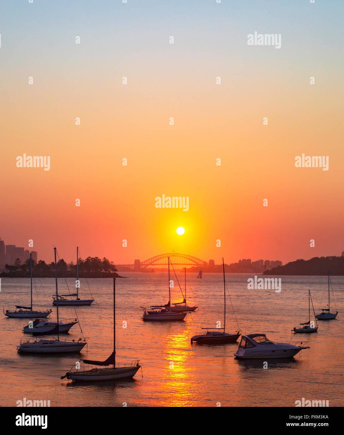 A beautiful sunset over Sydney Harbour Bridge reflected in the tranquil ...
