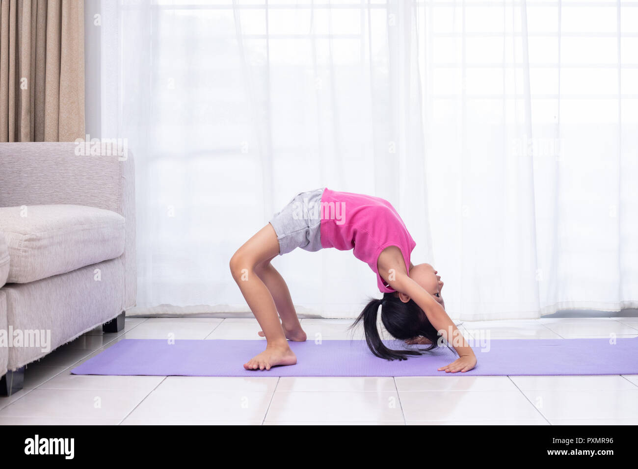 Asian Chinese little girl practicing yoga pose on a mat in the living ...
