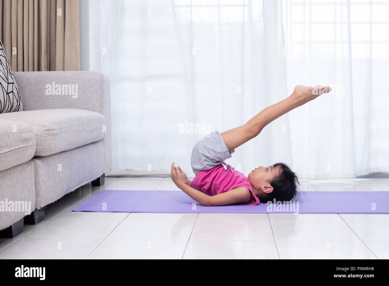 Asian Chinese little girl practicing yoga pose on a mat in the living ...