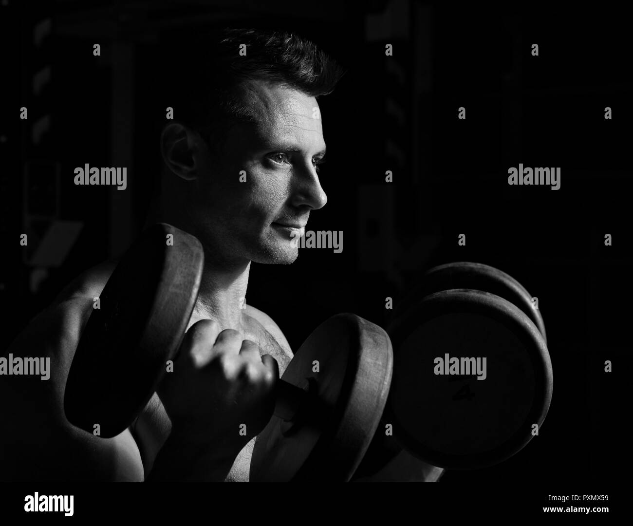 Handsome strong angry man doing the exercises with dumbbells on dark ...