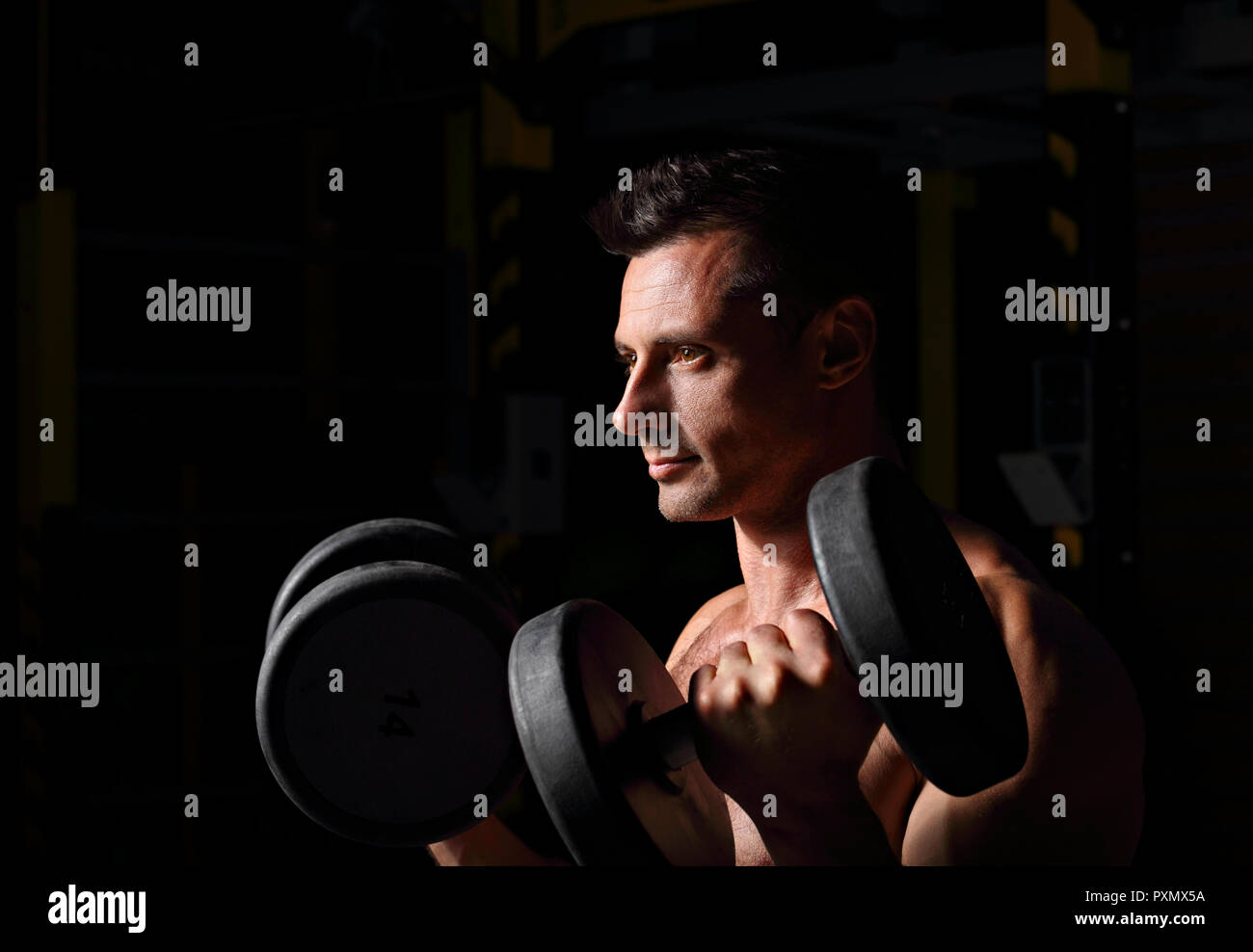 Handsome strong angry man doing the exercises with dumbbells on dark ...