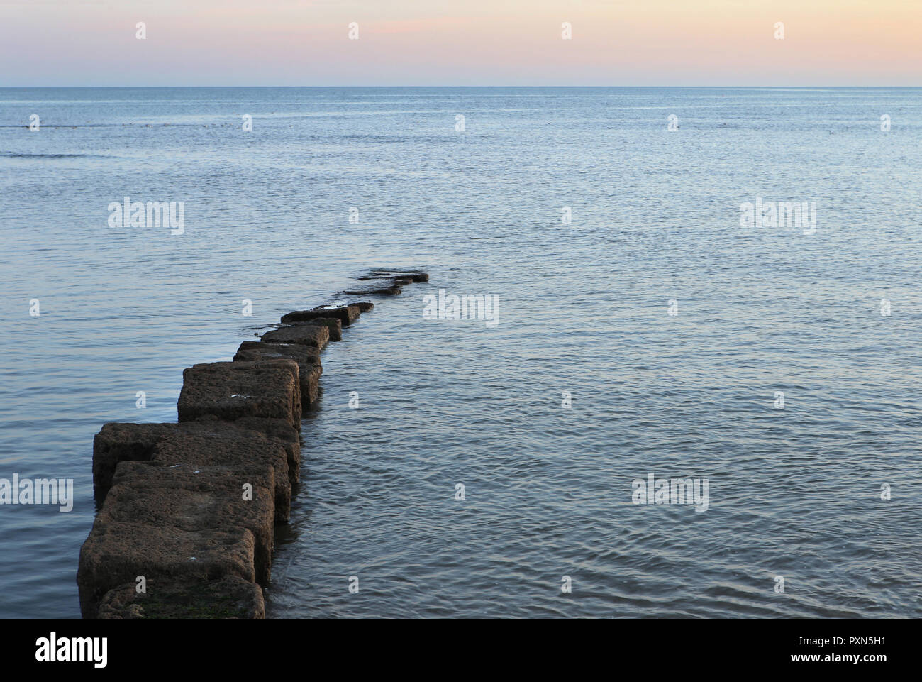 irregular stone jetty curves into twilight sea Stock Photo - Alamy