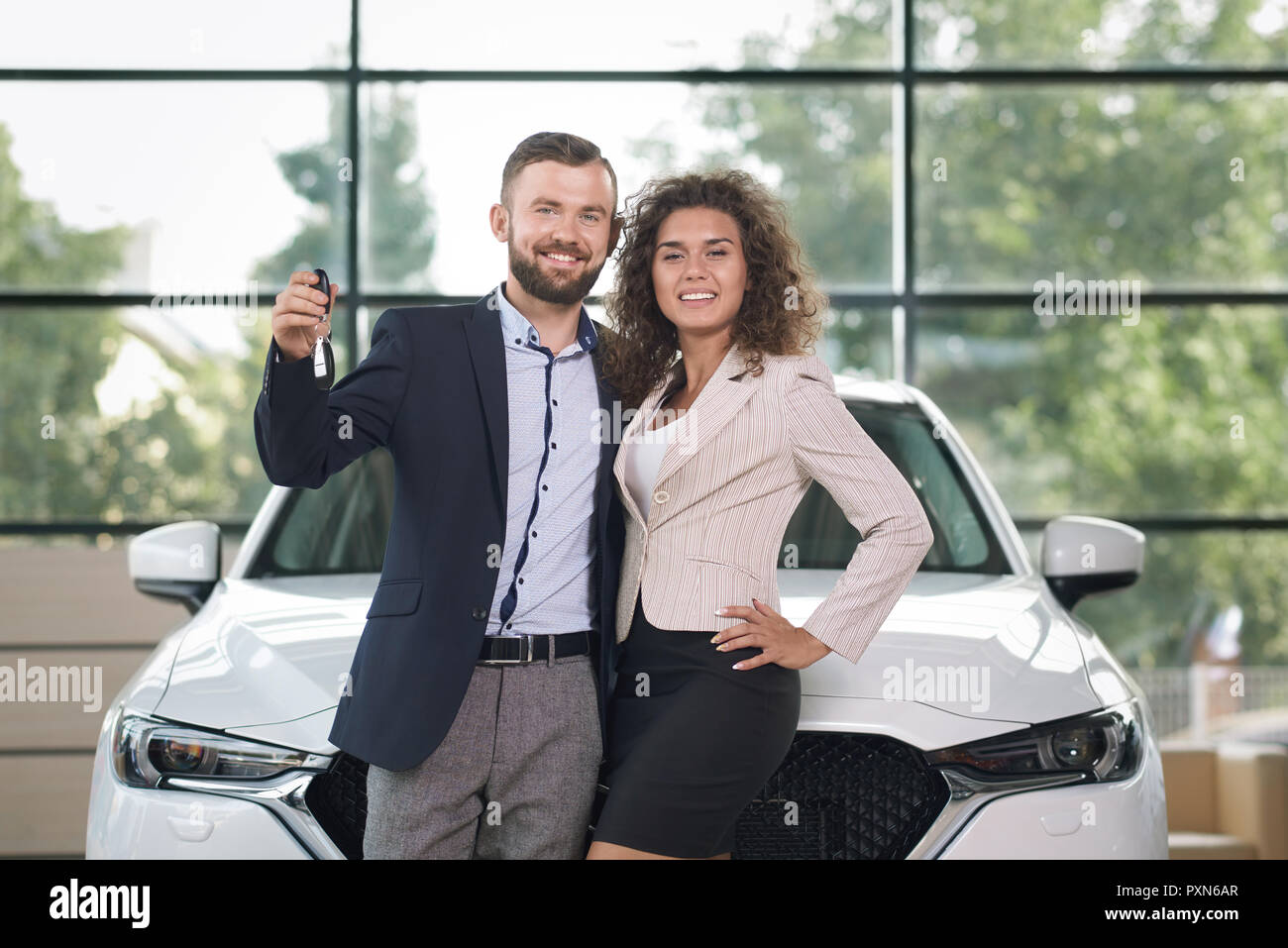 Happy husband and wife standing near white car, looking at camera and ...