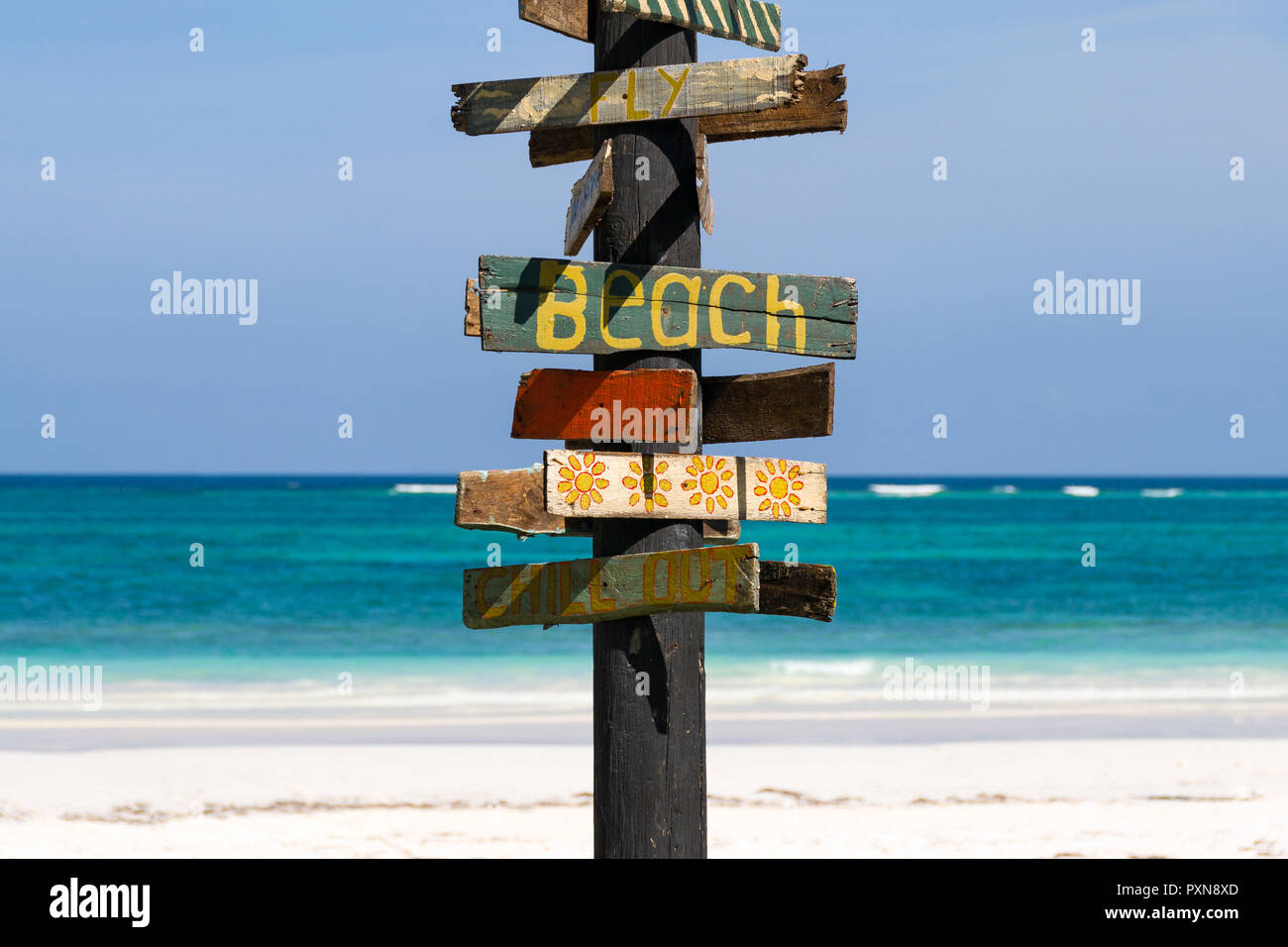 A signpost with Beach written on it with tropical beach and ocean in ...
