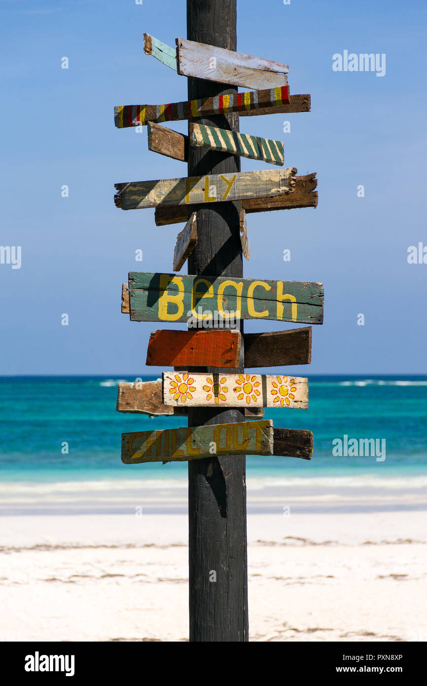 A signpost with Beach written on it with tropical beach and ocean in ...