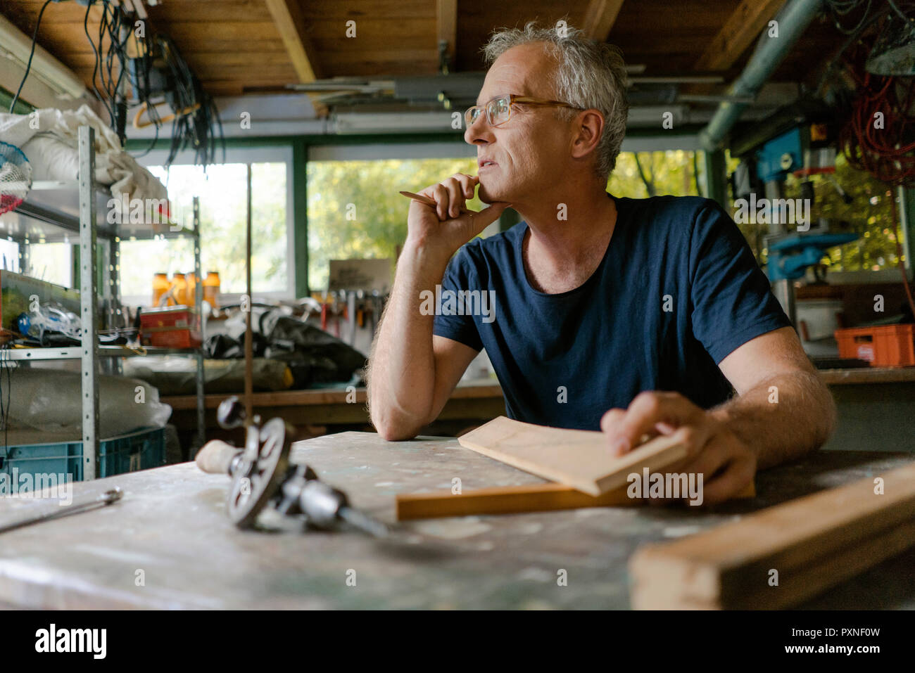 Mature man at workbench in his workshop thinking Stock Photo - Alamy