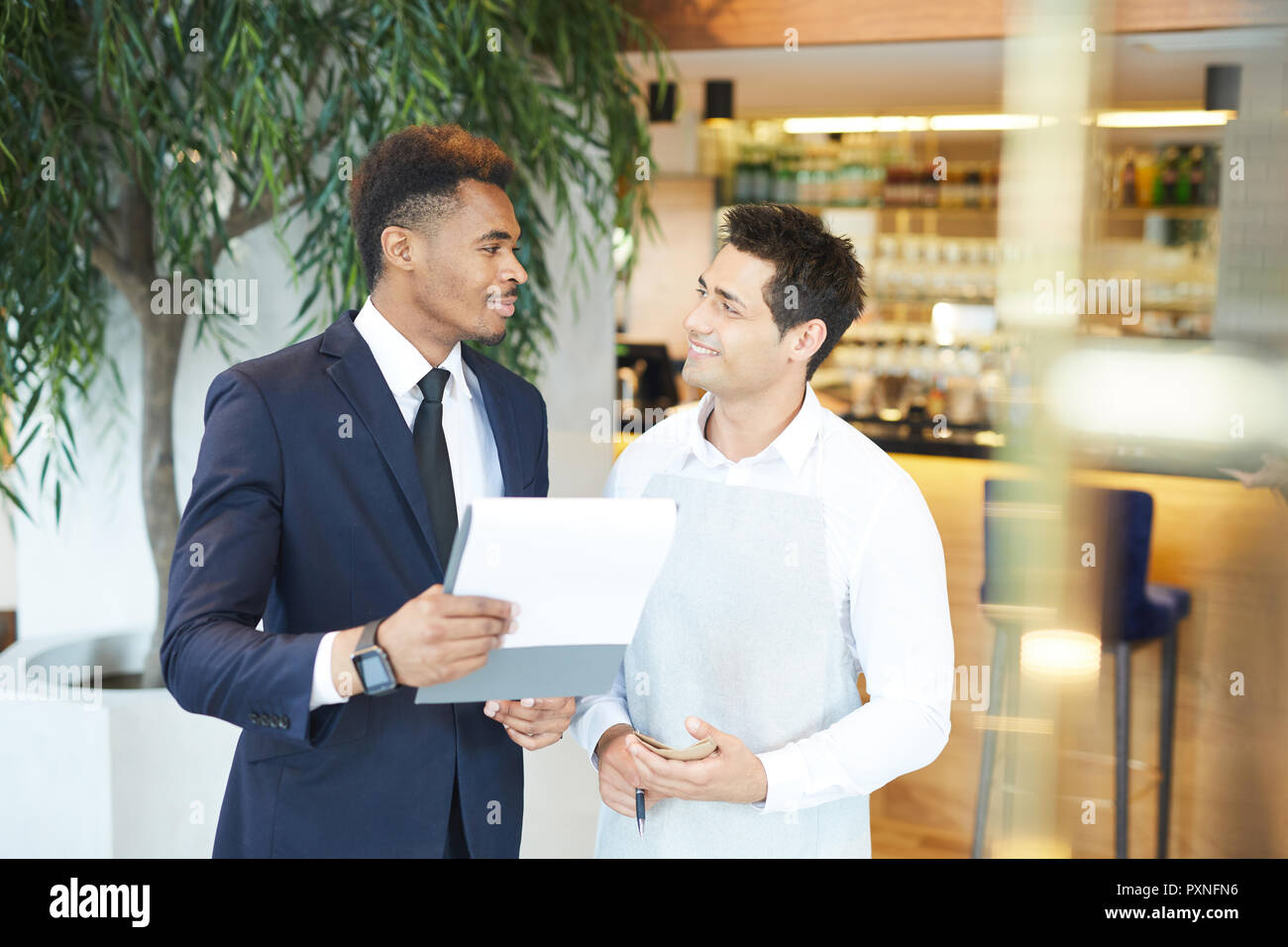 African businessman standing and discussing the menu with the waiter at ...
