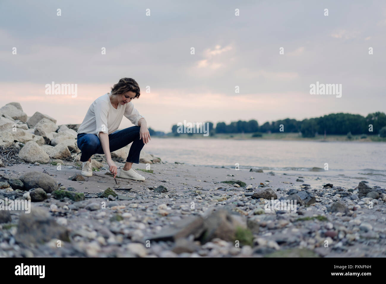 Woman crouching at the riverside, drawing in sand with a stick Stock ...