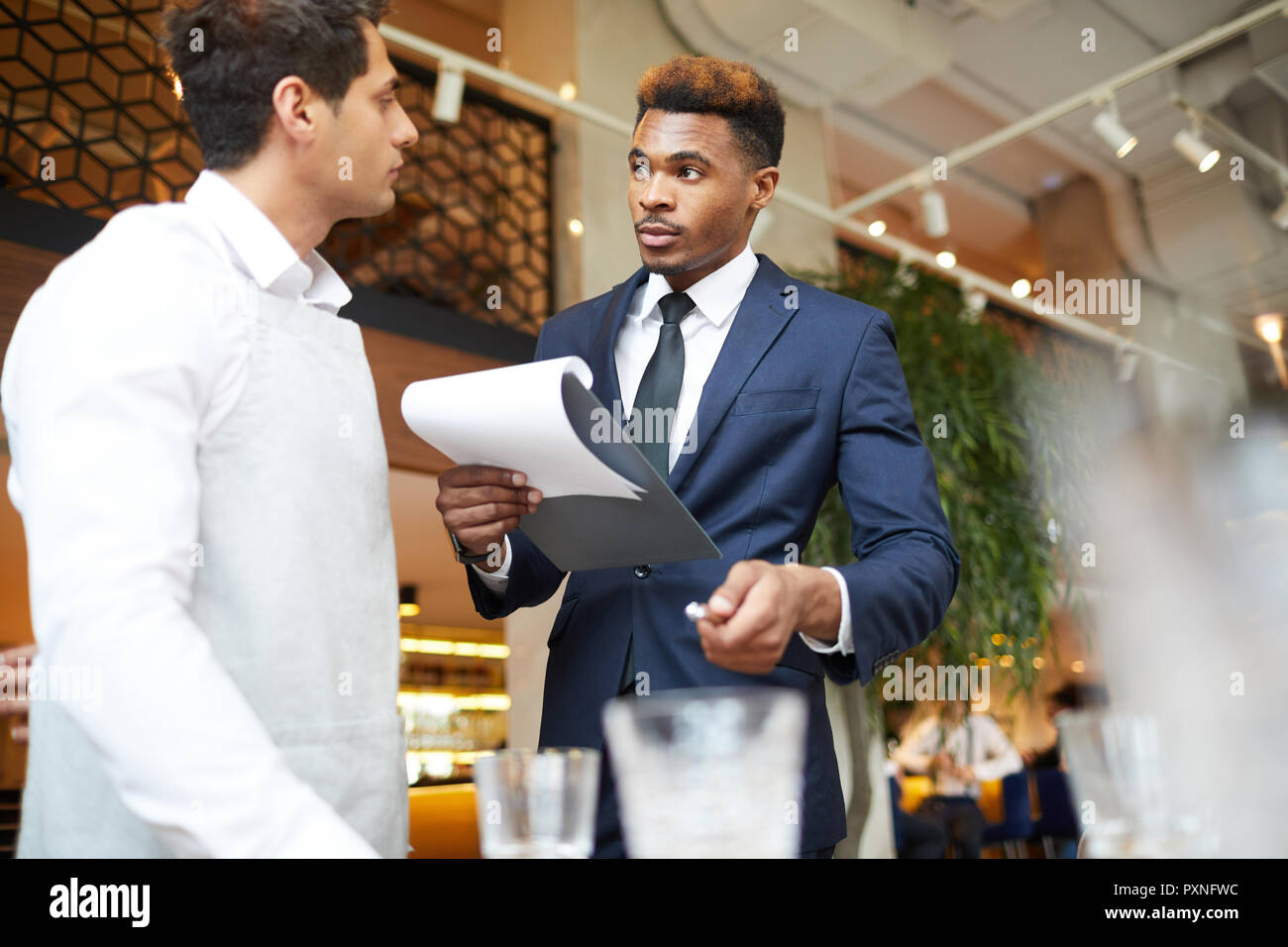 African young manager controlling the work of the waiter, the preparing ...