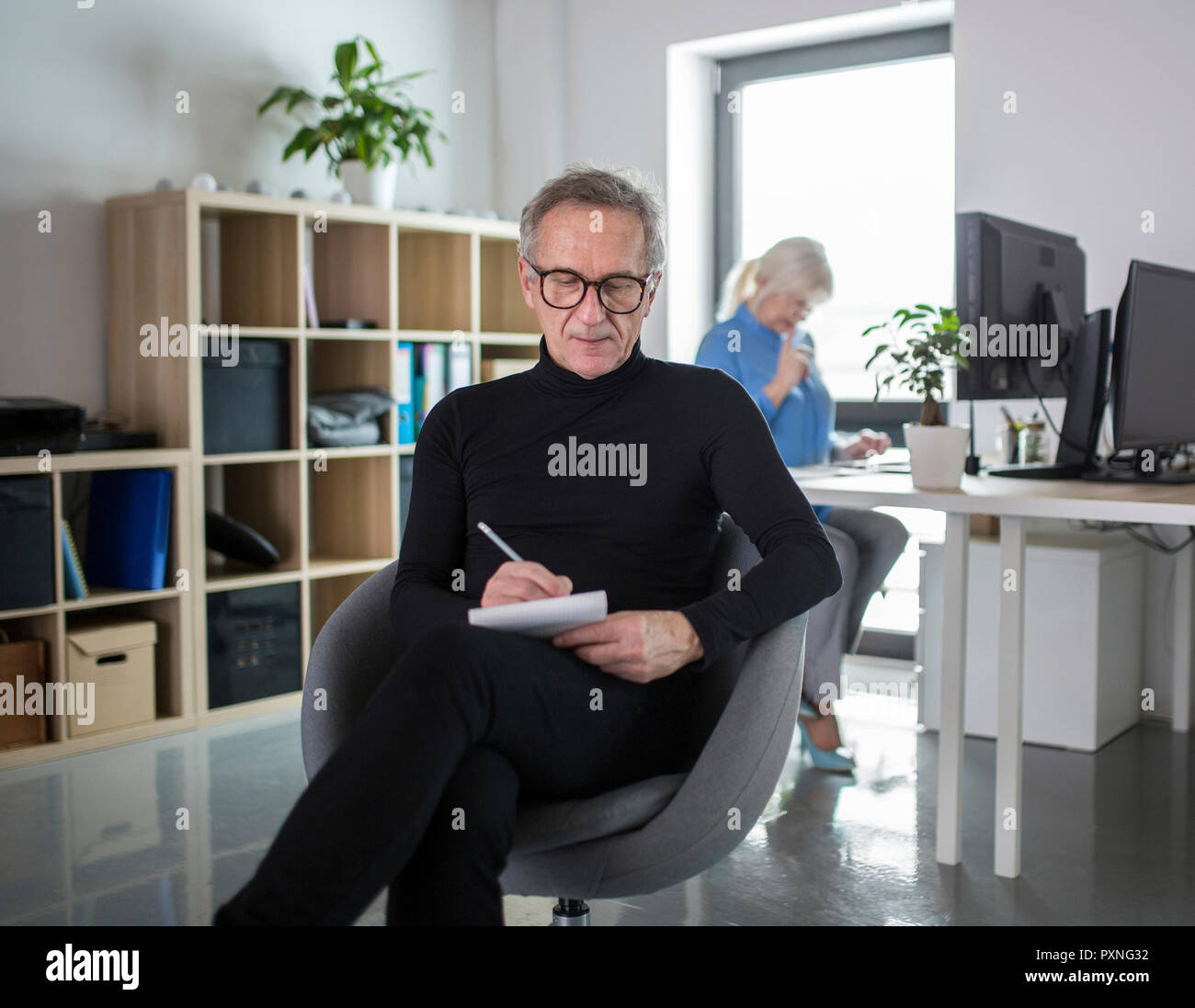 Senior man sitting office taking notes colleague working behind him hi ...