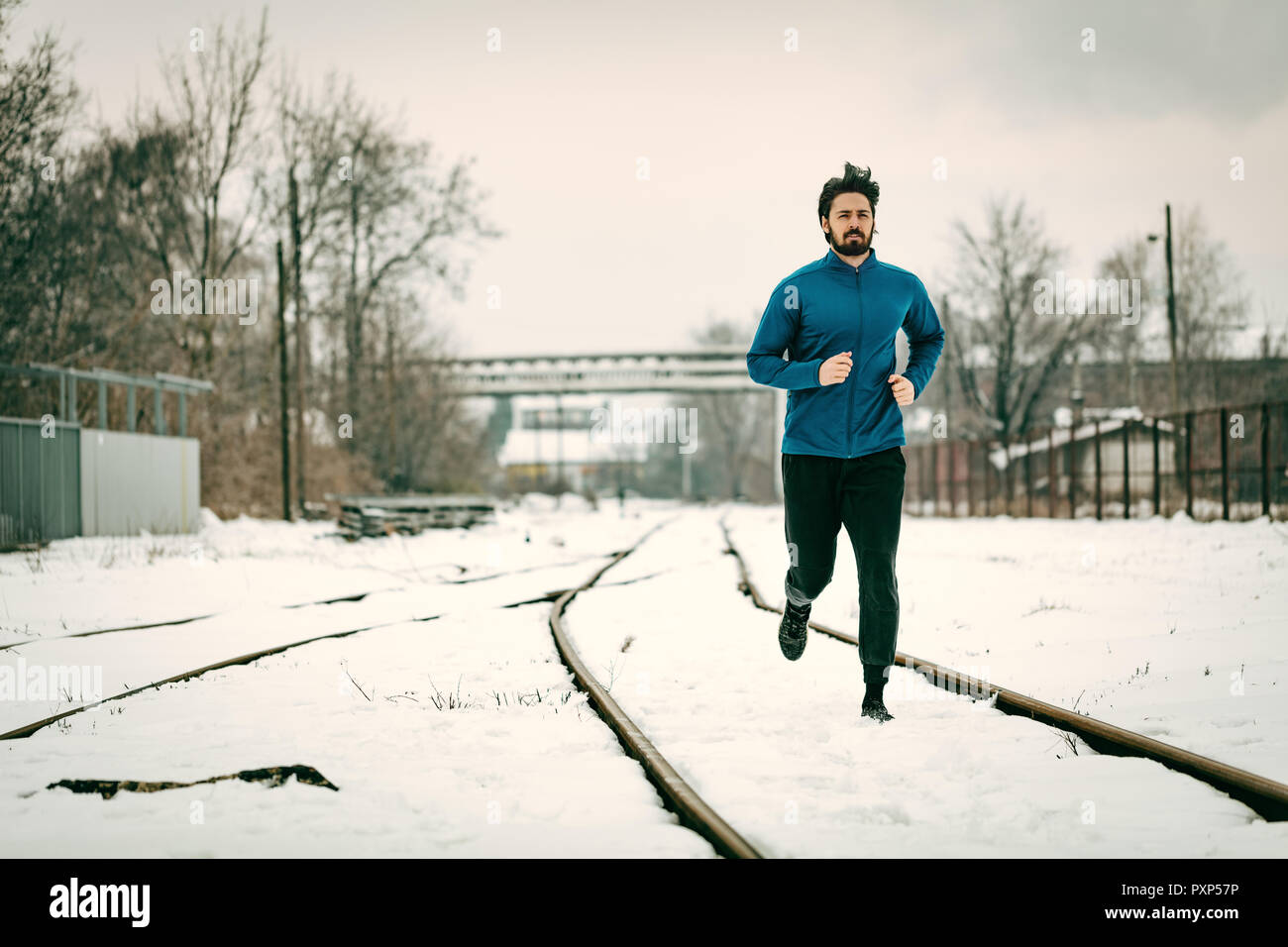 Active young man running and doing exercises across the old railroad ...