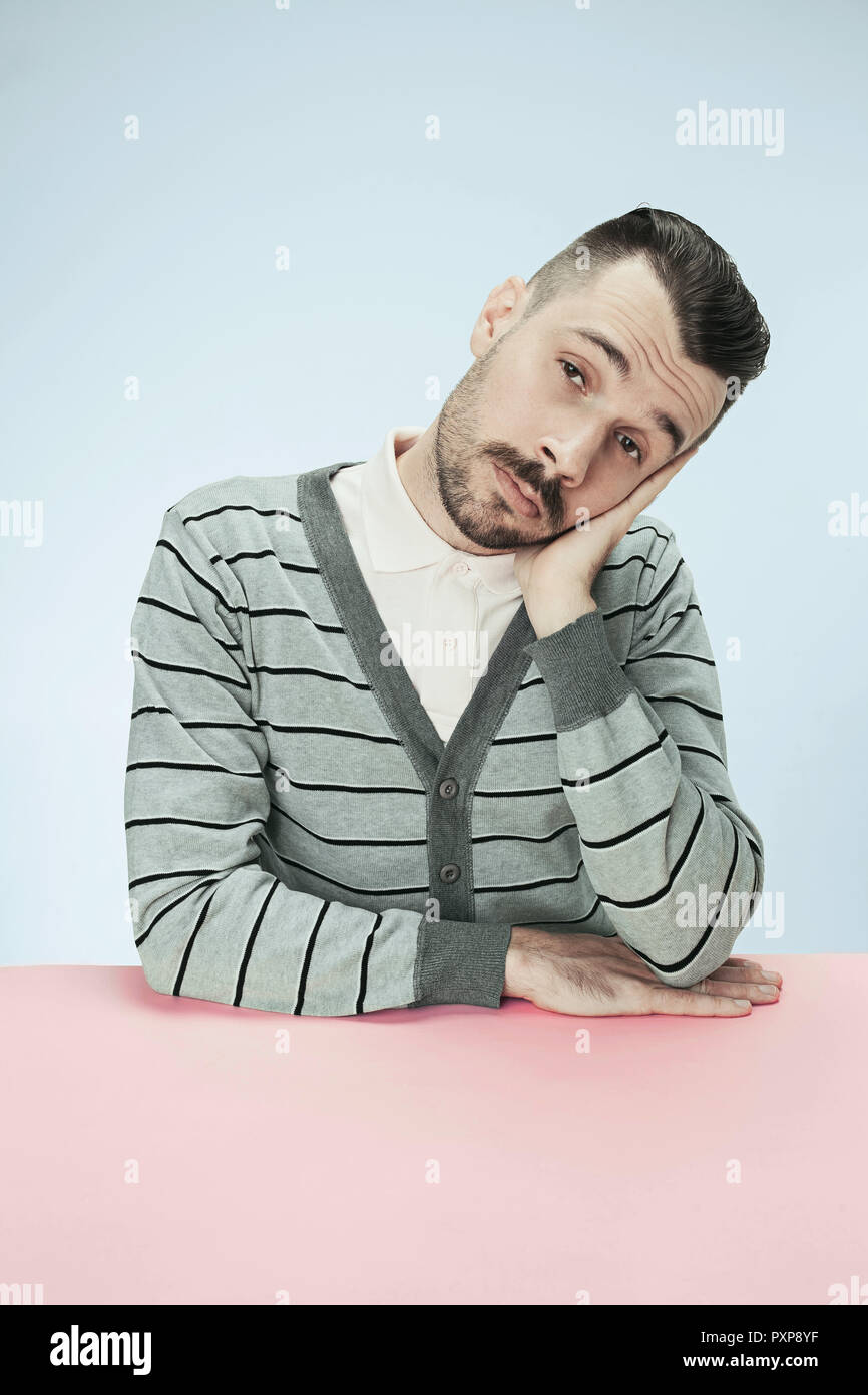 Serious, bored and dull business man sitting at table on blue studio ...