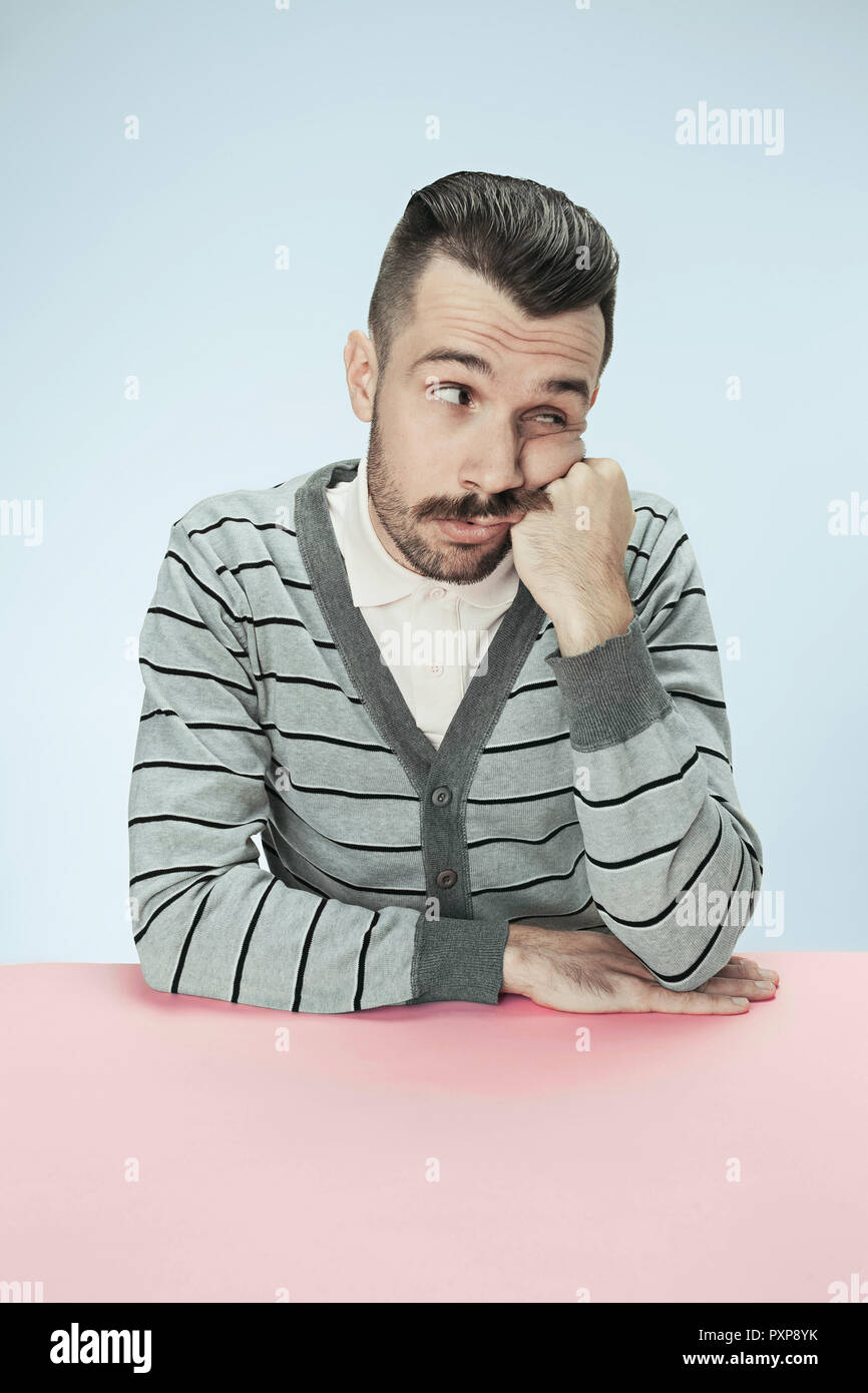 Serious, bored and dull business man sitting at table on blue studio ...