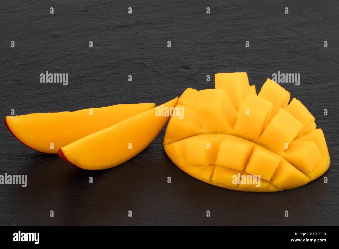 ripe mango cut in half and diced on dark slate Stock Photo - Alamy