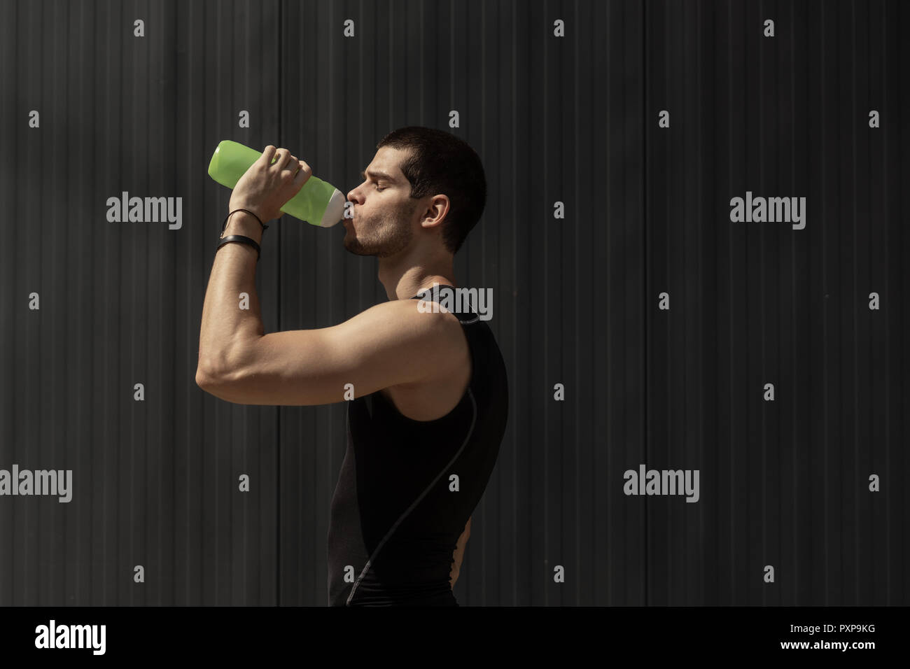 Sport model man drinking water from a plastic bottle on gray background ...