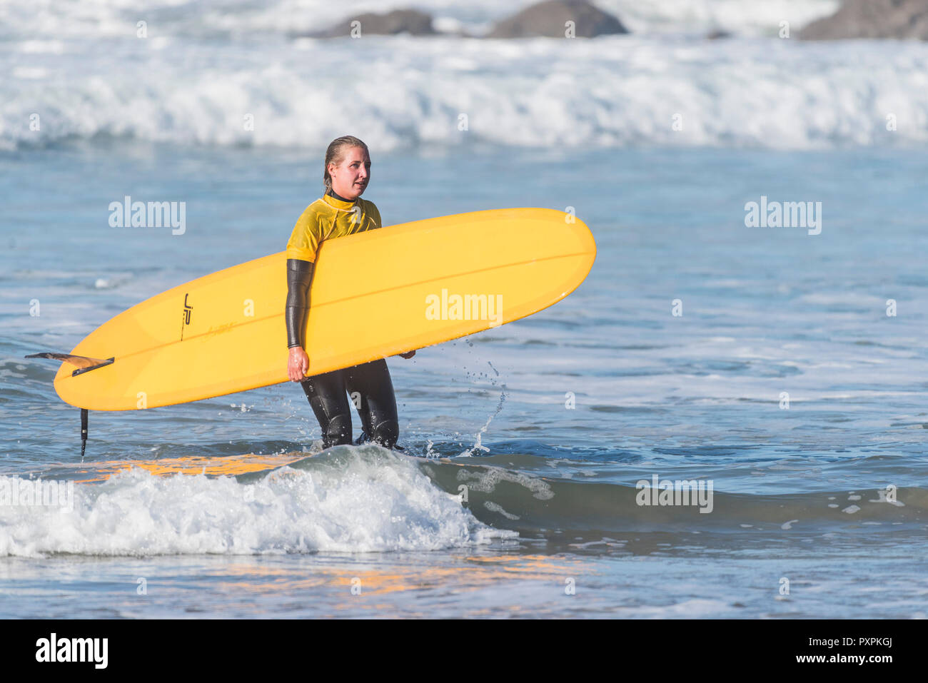 A tired surfer carrying her surfboard walking out of the sea at Fistral ...