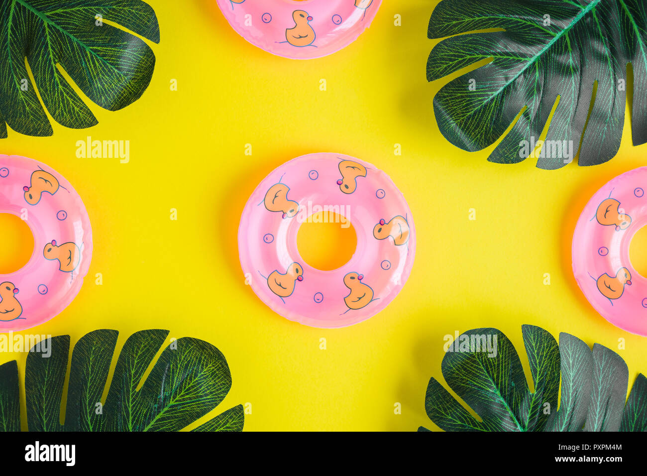 Tropical palm leaves and inflatable pool floats on yellow background ...