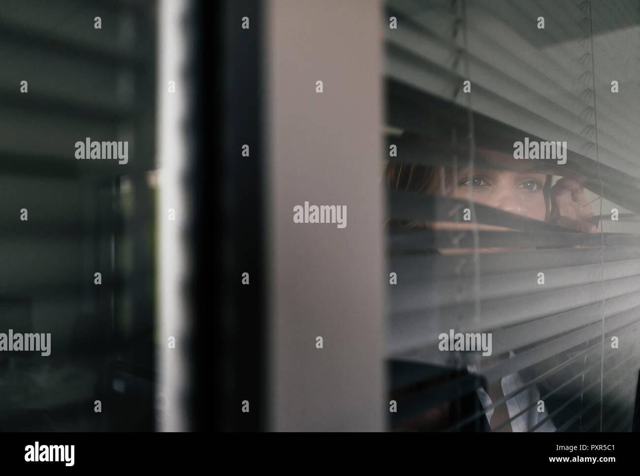 Woman standing by window, spying through blinds Stock Photo - Alamy