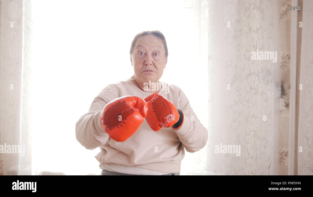 An old senior women boxing in red gloves, looking aggressively funny ...