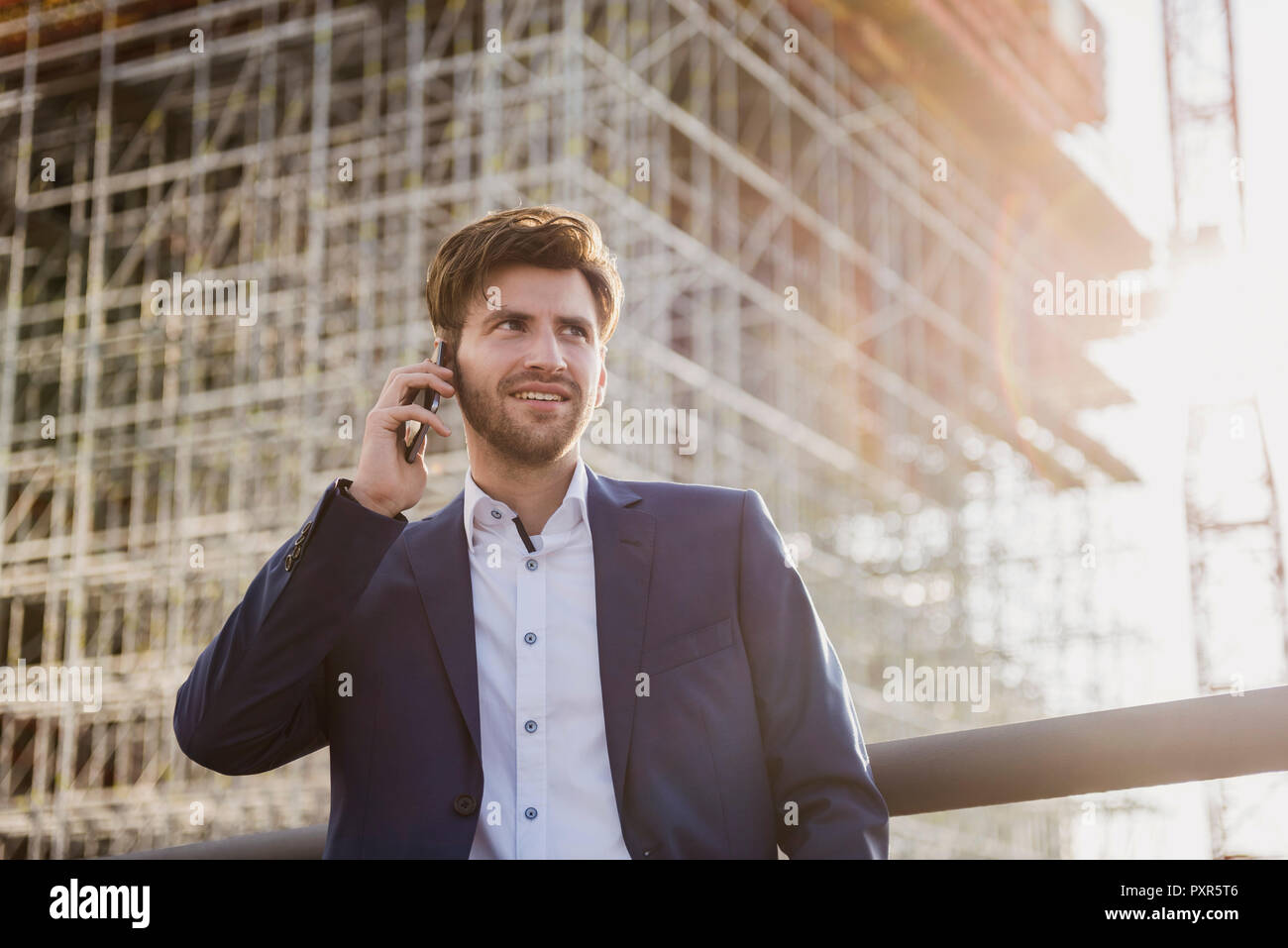 Businessman standing on bridge in front of construction site talking on ...