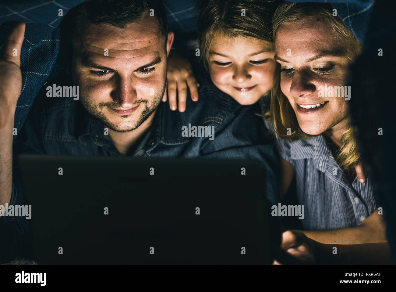 Happy family hiding under blanket, watching film on laptop Stock Photo ...