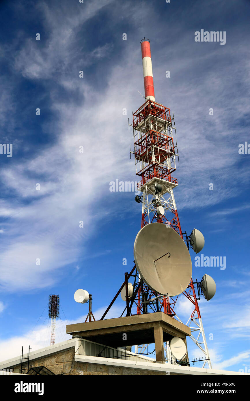 Several kind of communication antennas and a red and white tower against deep mountain blue sky ...