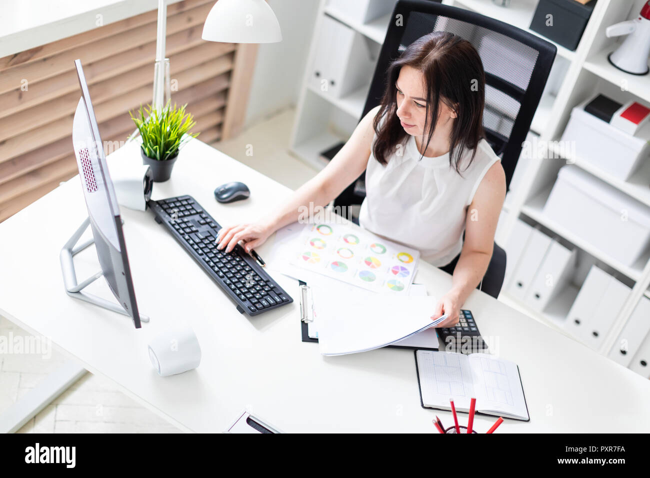 A young girl sitting in the office at a computer Desk and working with ...