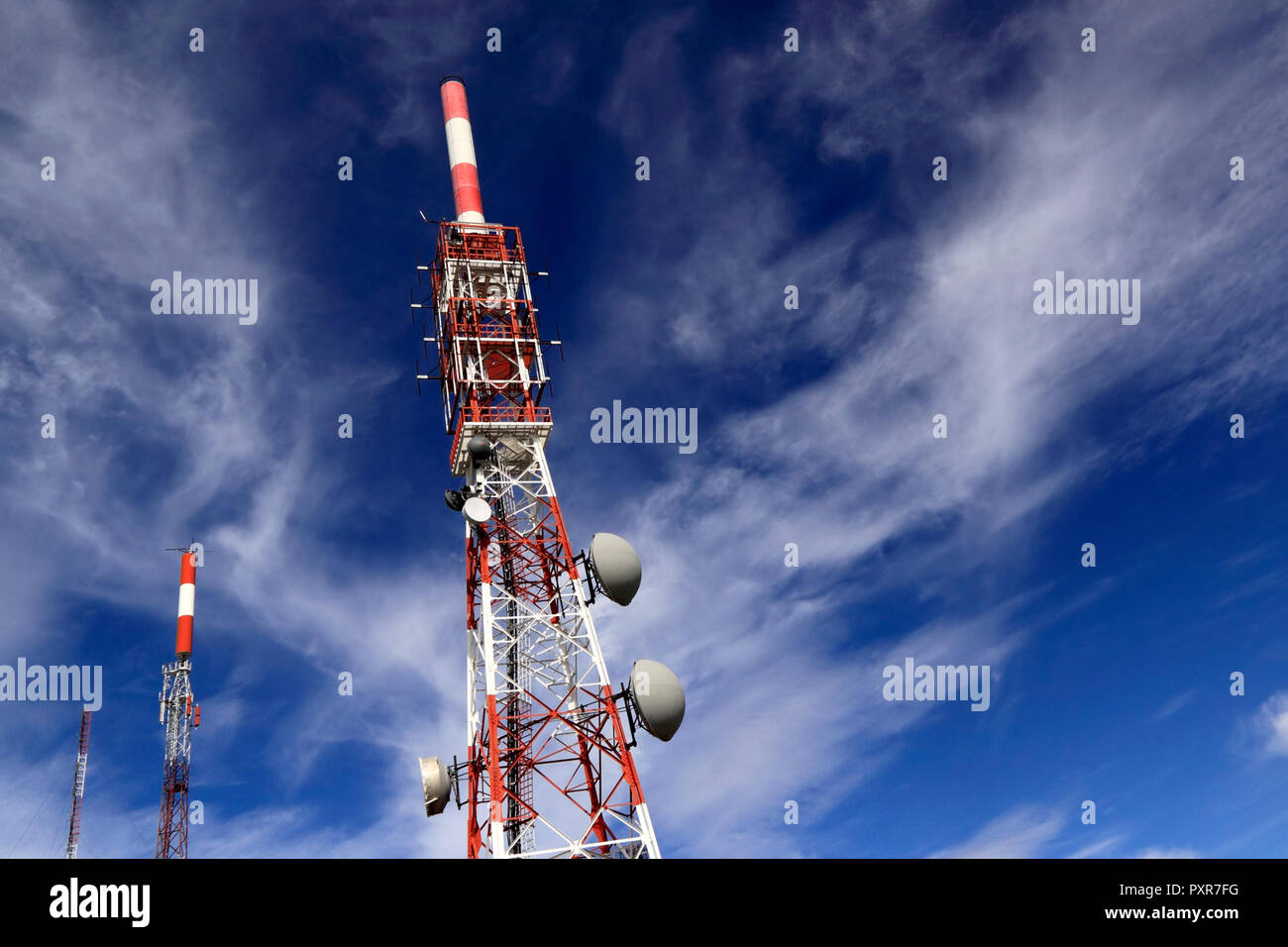 Several kind of communication antennas and a red and white tower against deep mountain blue sky ...