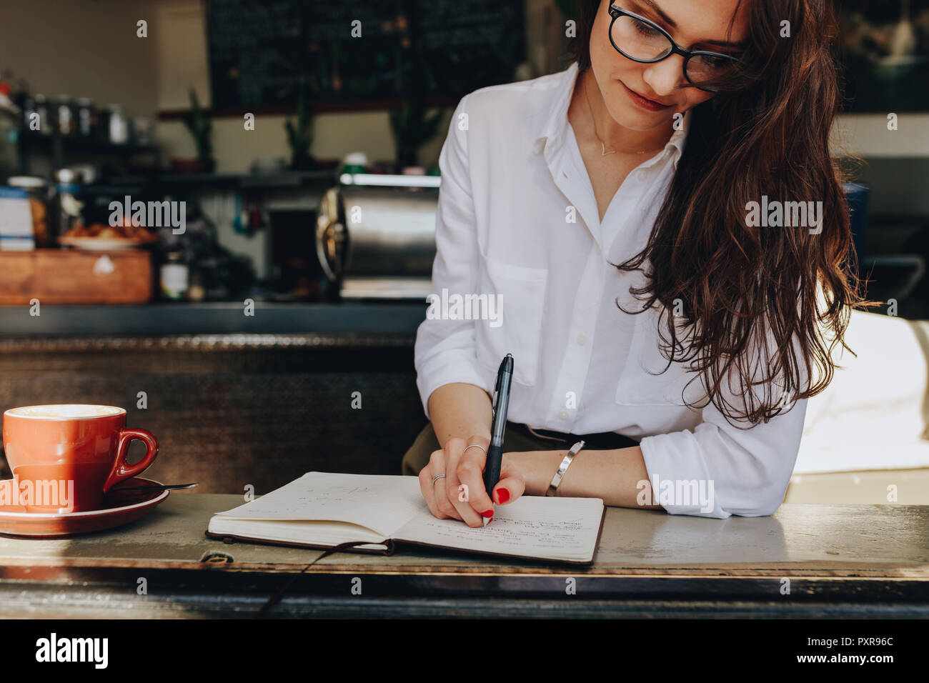 Woman in the cafe writing notes in a book while sitting at coffee shop ...