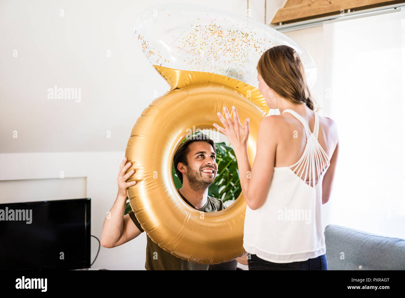 Smiling man looking at girlfriend through large inflatble ring at home ...