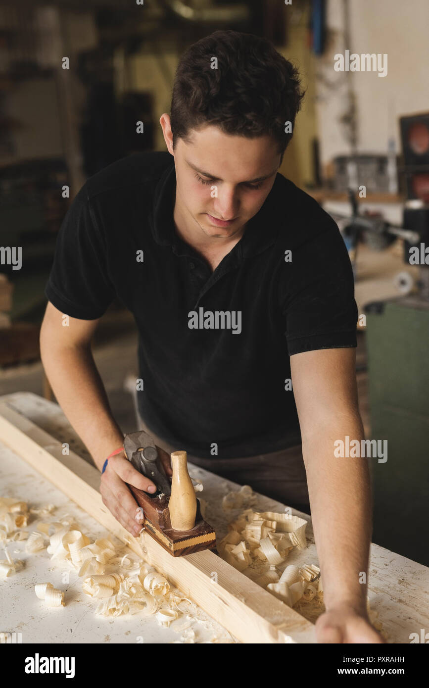 Carpenter using plane on piece of wood in workshop Stock Photo - Alamy