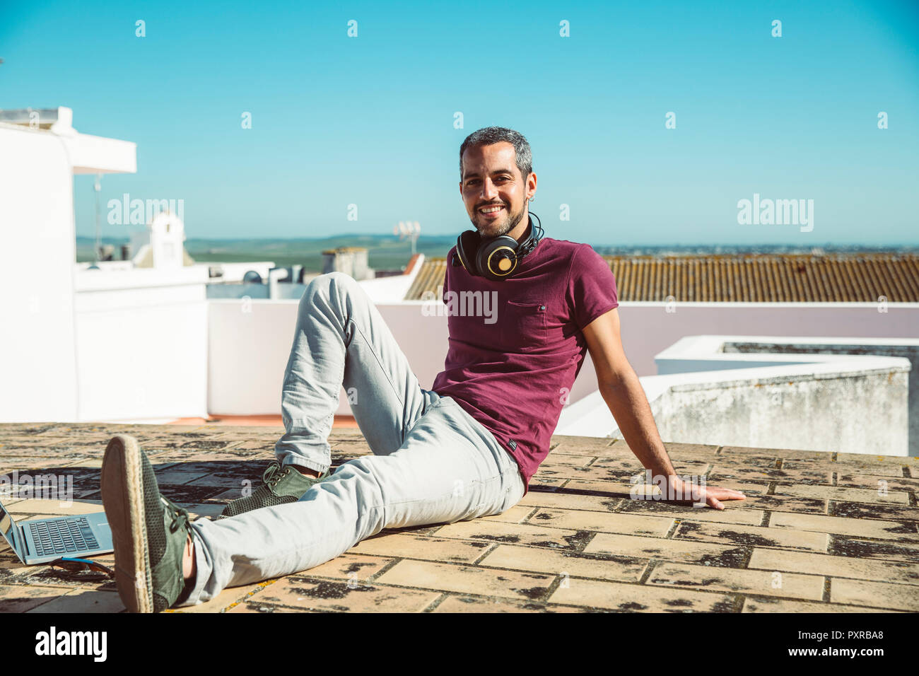 Smiling man sitting on roof, enjoying summer Stock Photo - Alamy