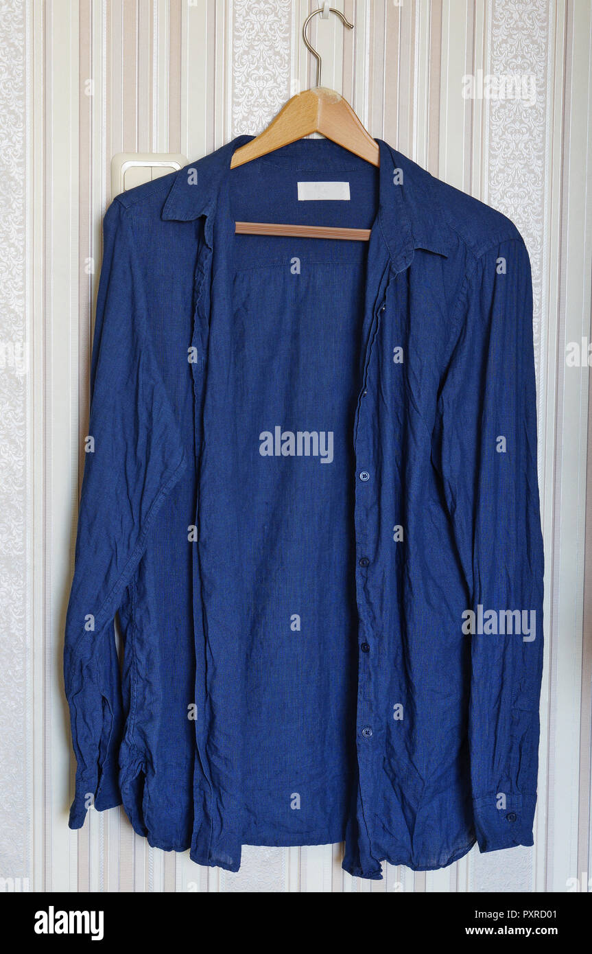 Women's cotton blue shirt on wooden hanger hanging on the wall of the ...