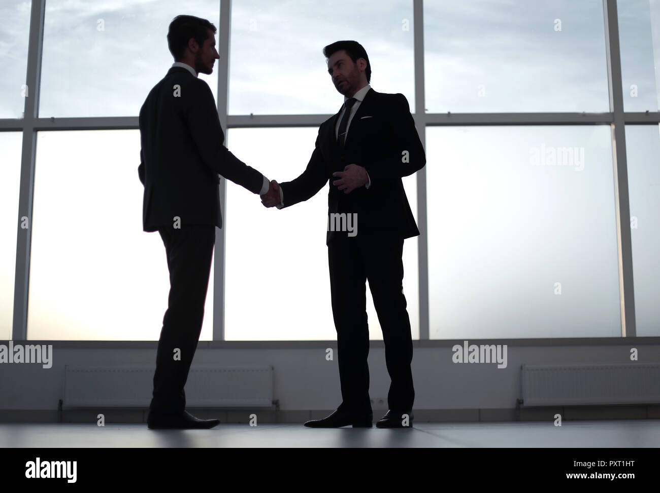 businessmen shake hands, standing near a large office window Stock ...