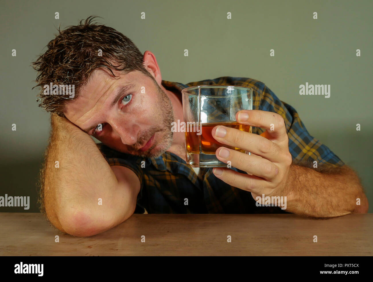 isolated portrait of young messy depressed alcoholic man having a drink looking at whiskey glass ...